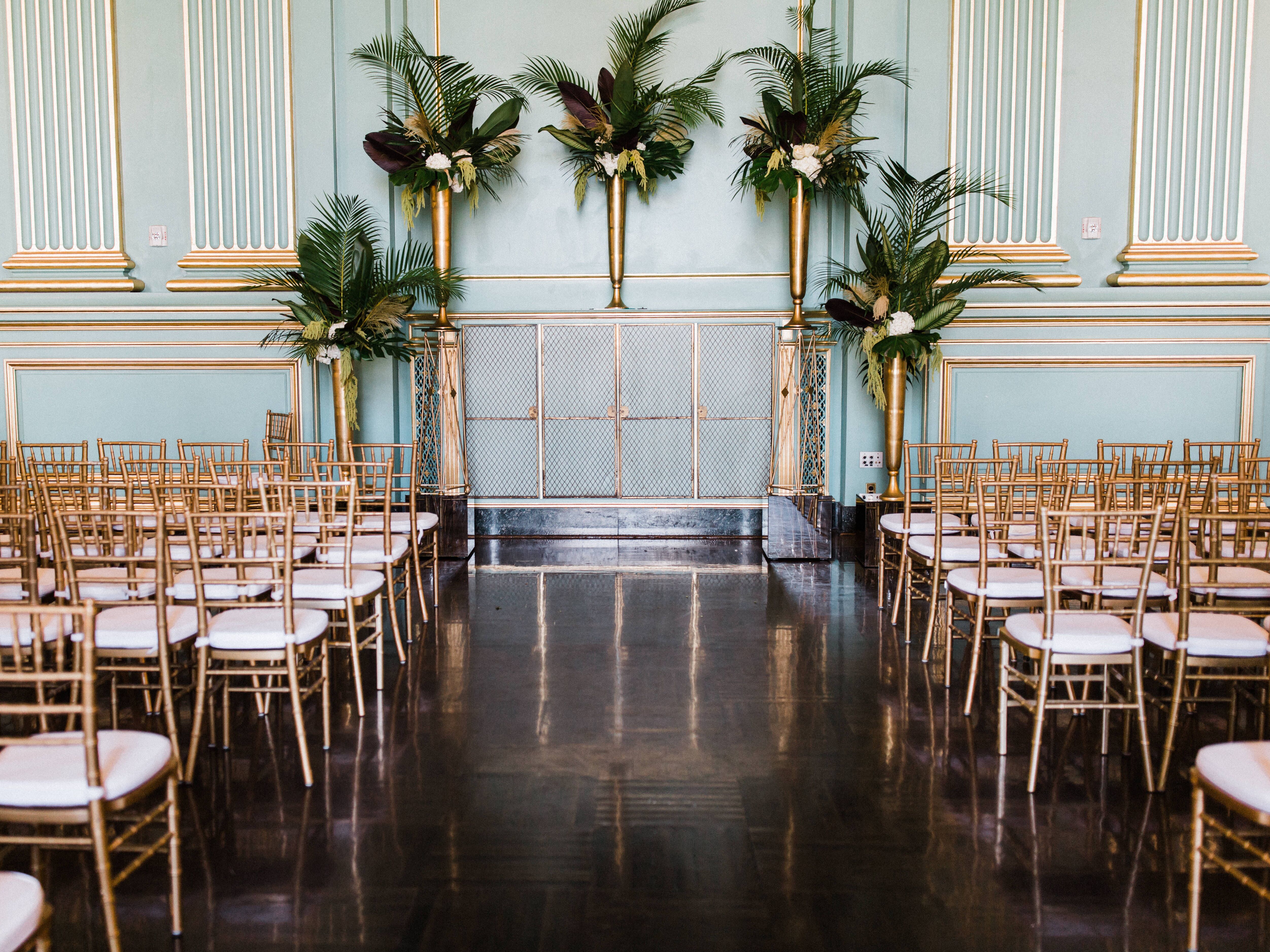 Modern Ceremony Site with Gold Chairs and Tropical Leaves