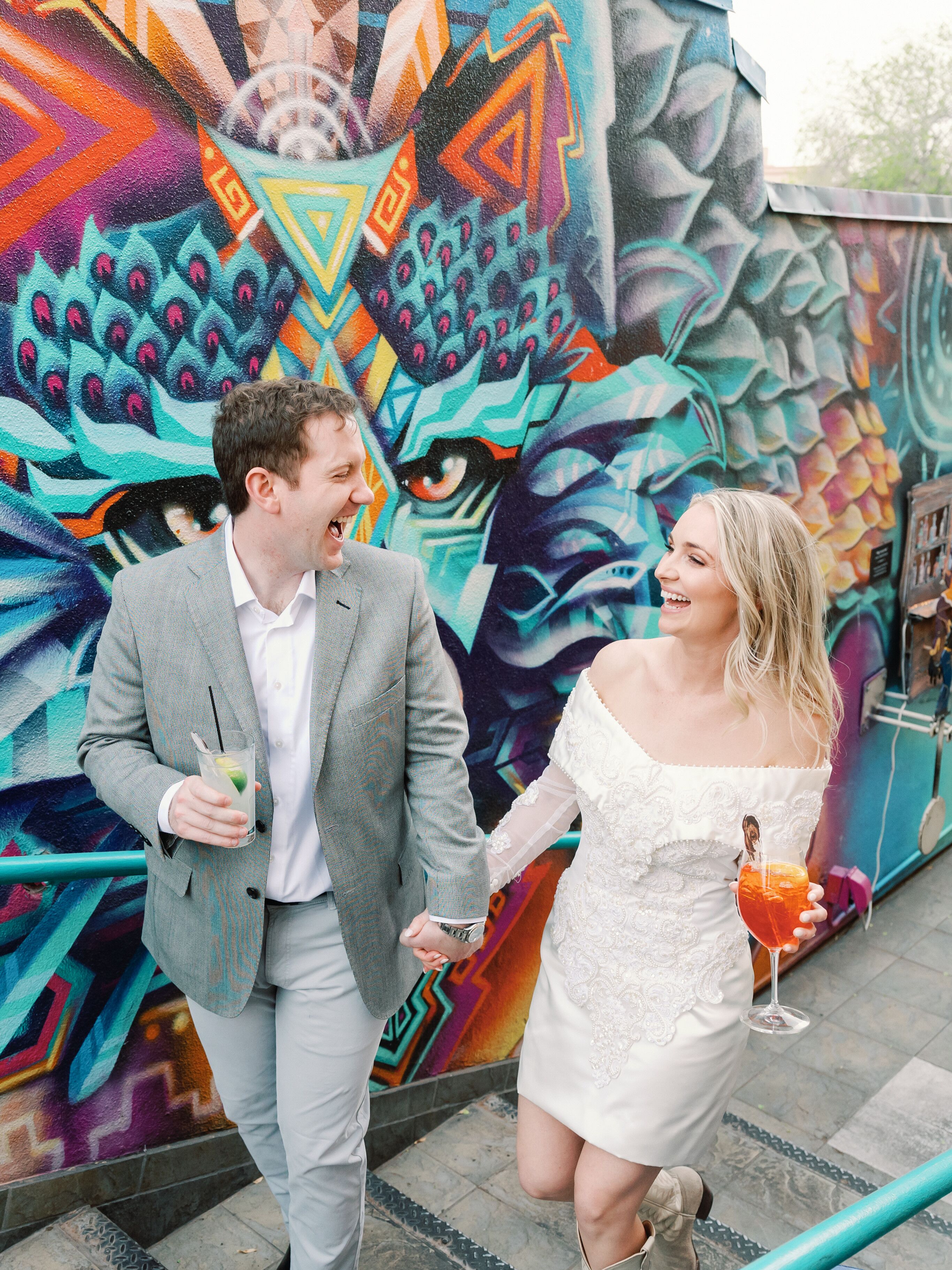 Bride In Mini Dress And Groom In Gray Suit Sip Cocktails At Colorful