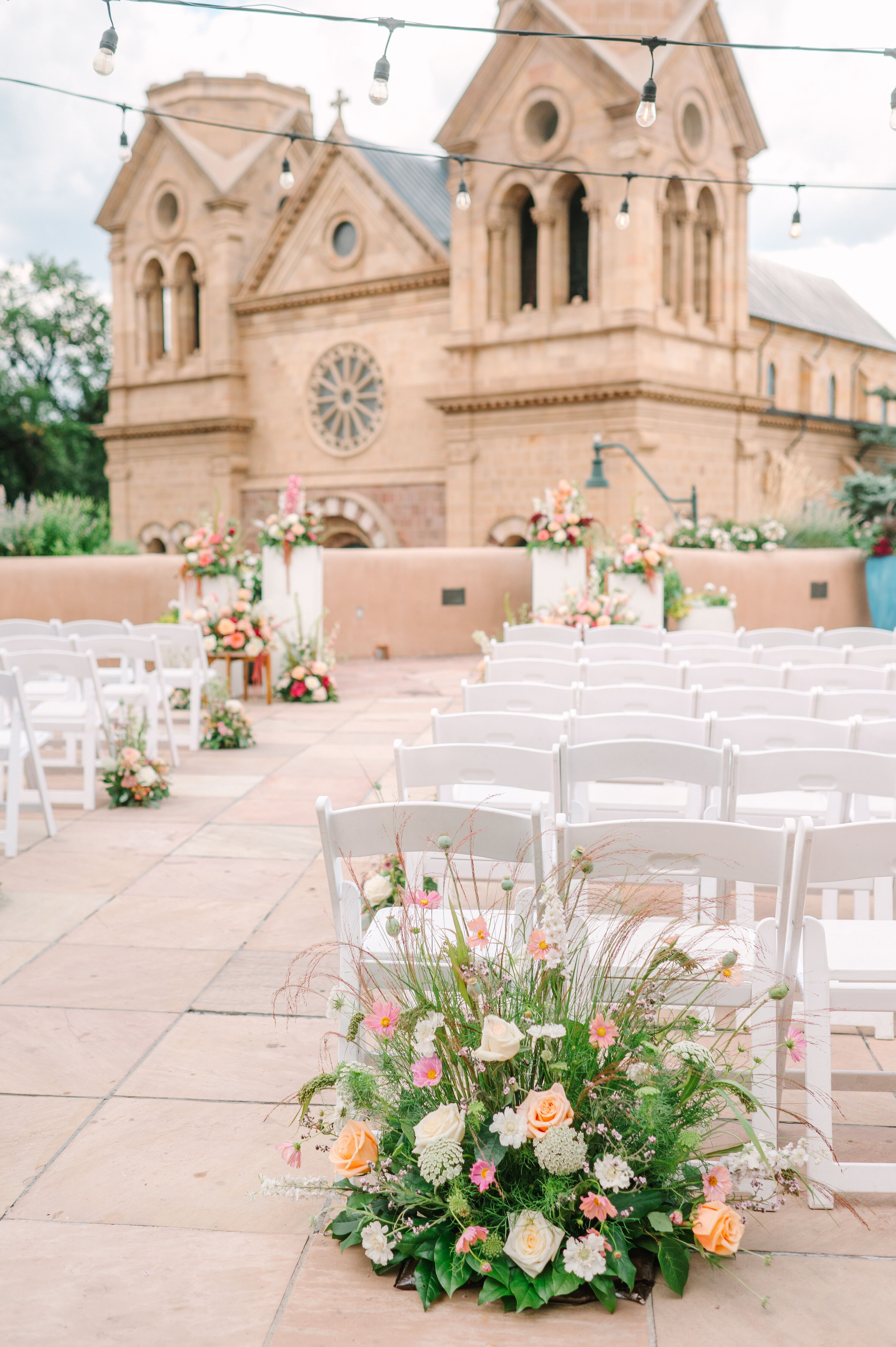Historic La Fonda Venue With White Ceremony Chairs and Floral Aisle Decor
