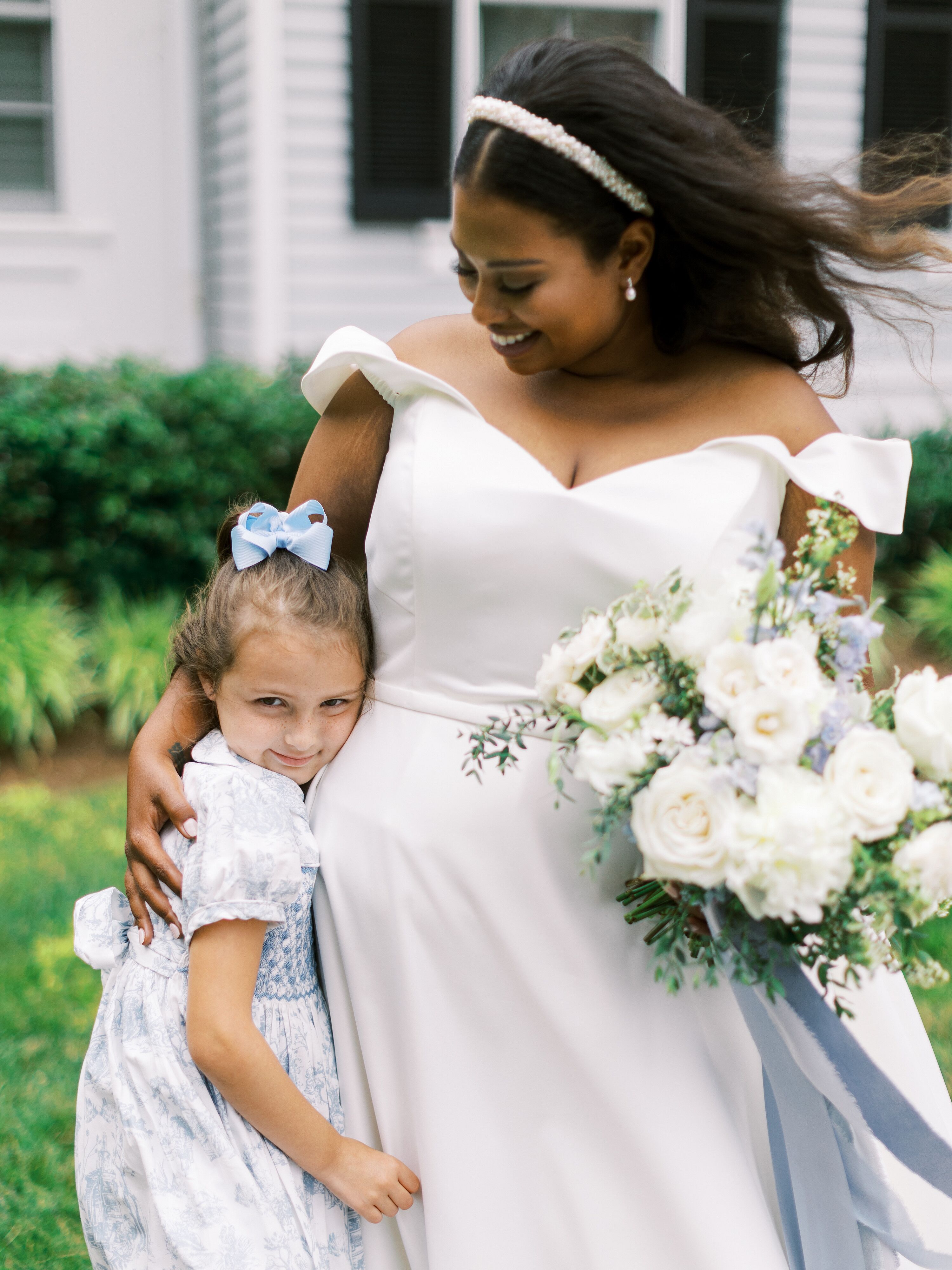 Bride in Sleek Wedding Gown Embracing Flower Girl in White-and-Blue Dress